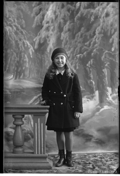 Smaidīga meitene mētelī pozē uz gleznota fona | Europeana